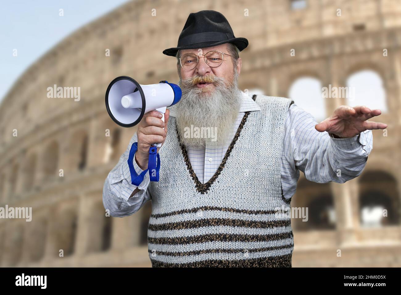 Senior bearded man talking into megaphone while standing on blurred ...