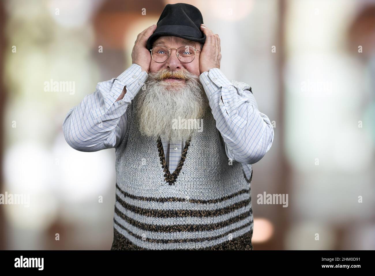 Cheerful amazed old man with gray beard holding hands on head with shock expression. Abstract ...