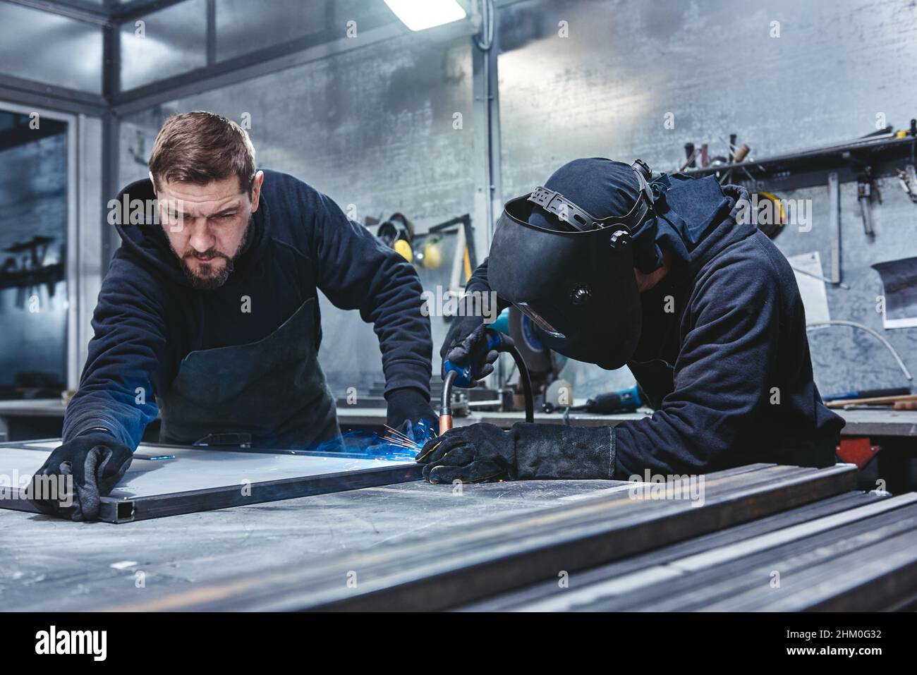 Profesional welder in protective uniform and mask welding metal frame ...