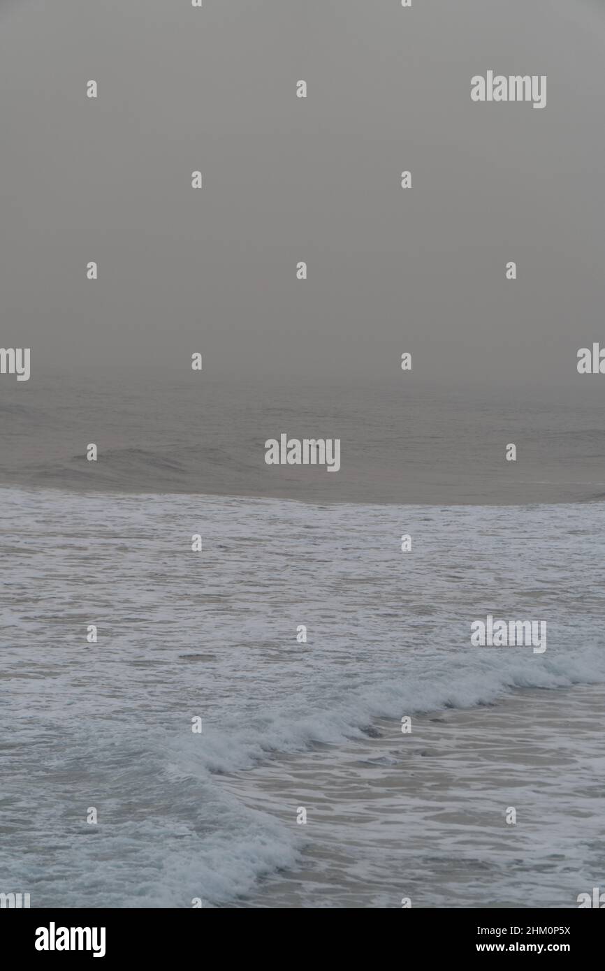 Vertical distant view of the ocean, waves and the surfer on a gloomy ...