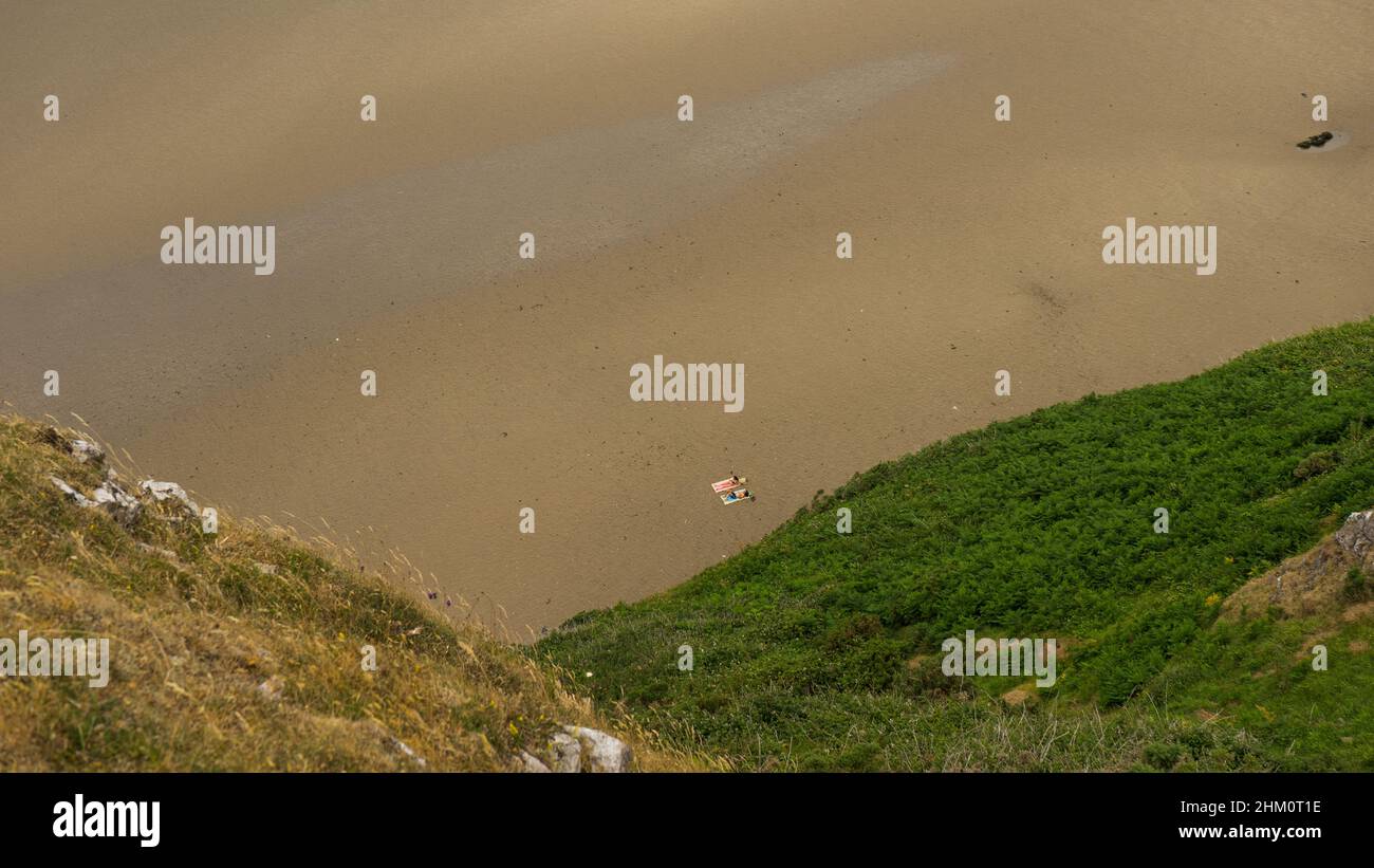 Two sunbathers on towels, on a deserted beach in the Gower Peninsula ...