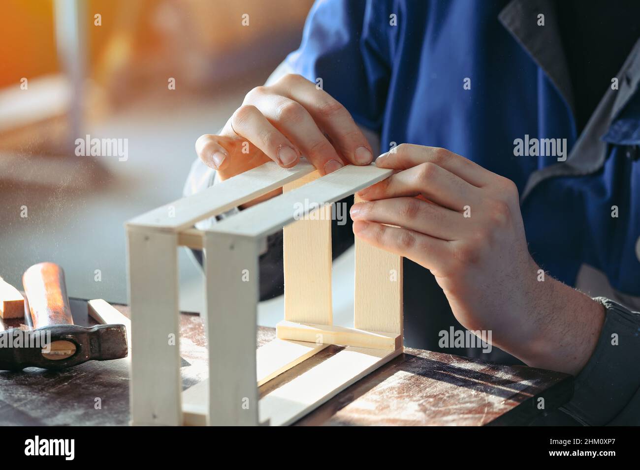 Young Caucasian carpenter in working clothes makes wooden boxes in ...