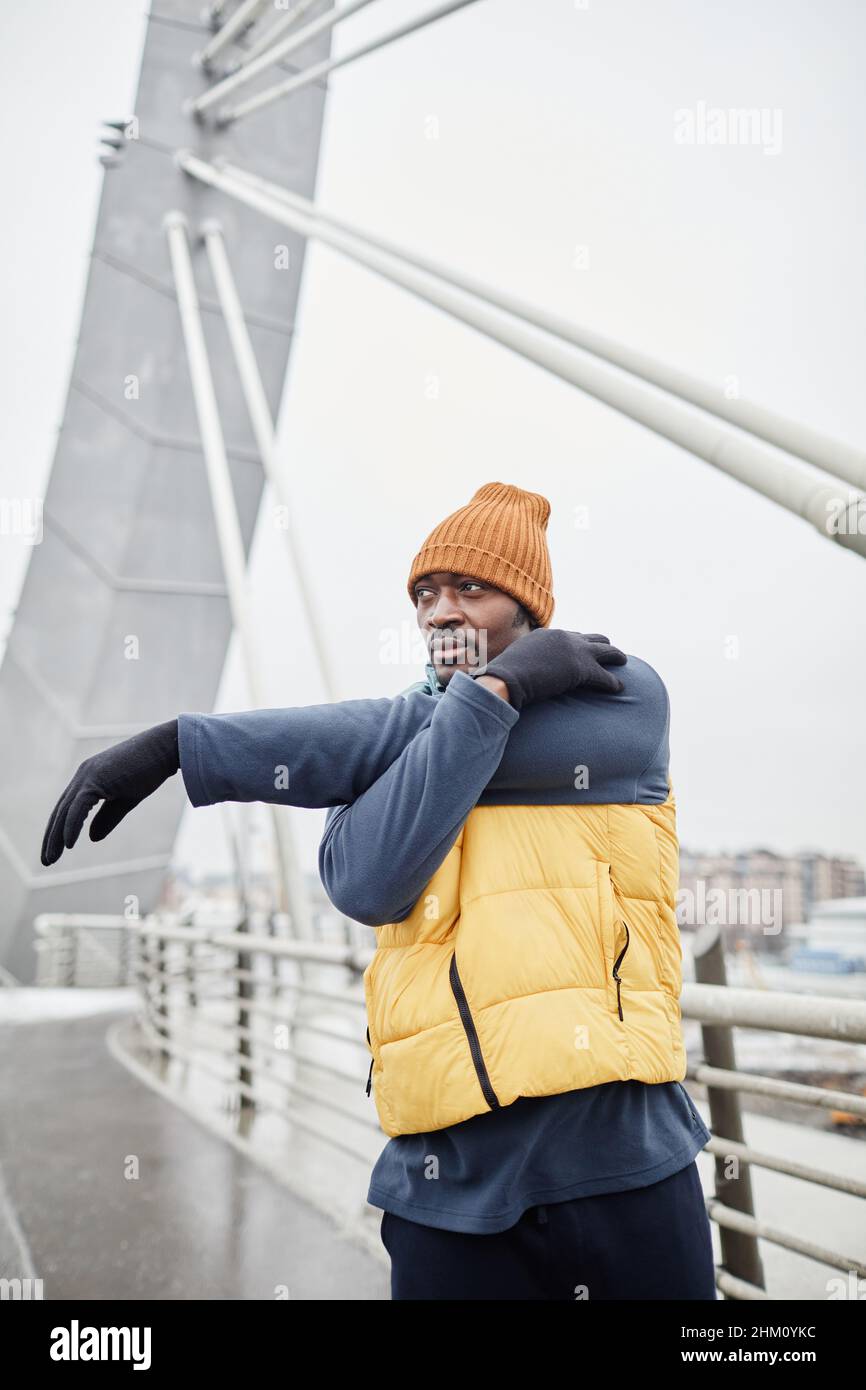 Active young man in sleeveless jacket, cap, gloves and tracksuit ...