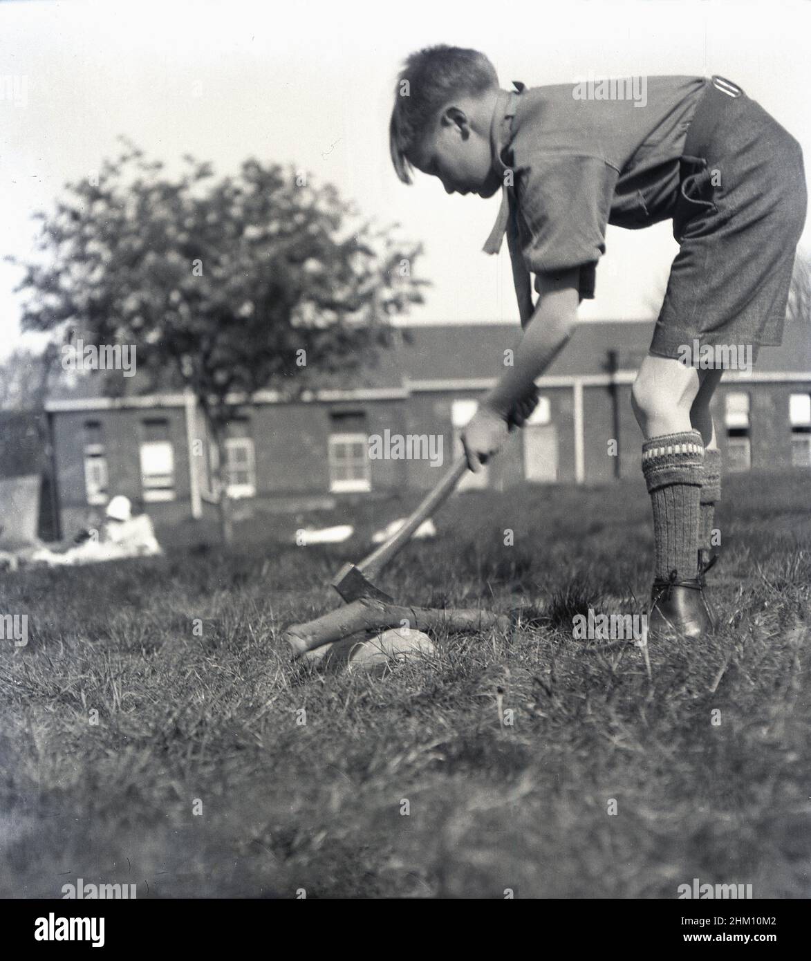 1942, historical, a cub scout in his uniform using an axe, to chop a ...