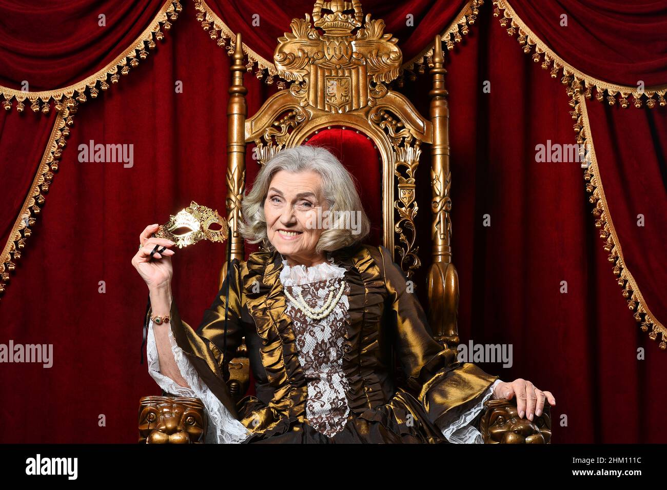 Happy beautiful senior queen with mask on throne Stock Photo - Alamy