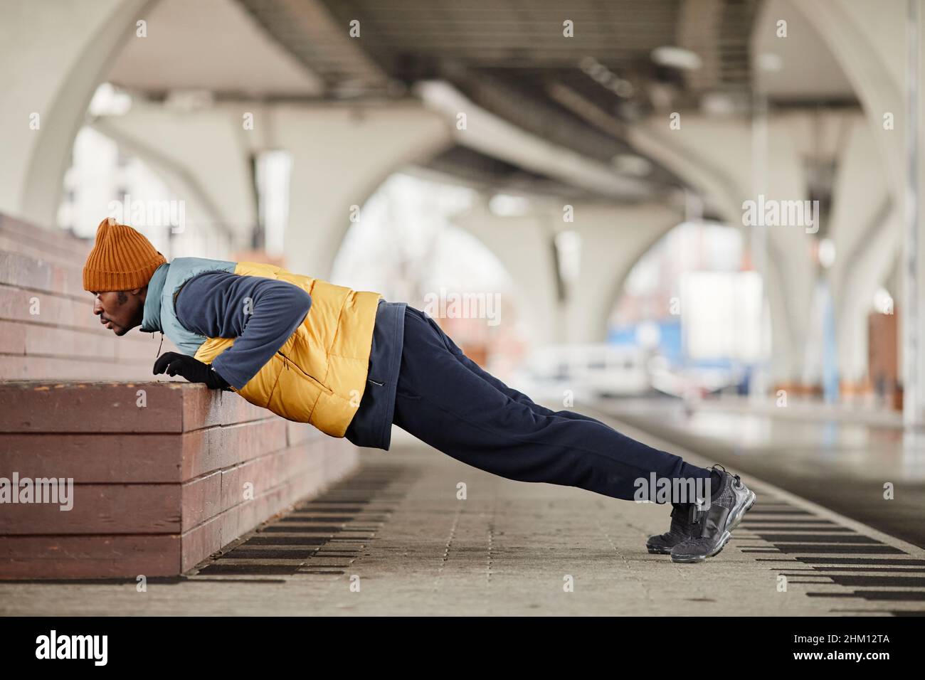Young African American athlete doing push ups against brick step while ...