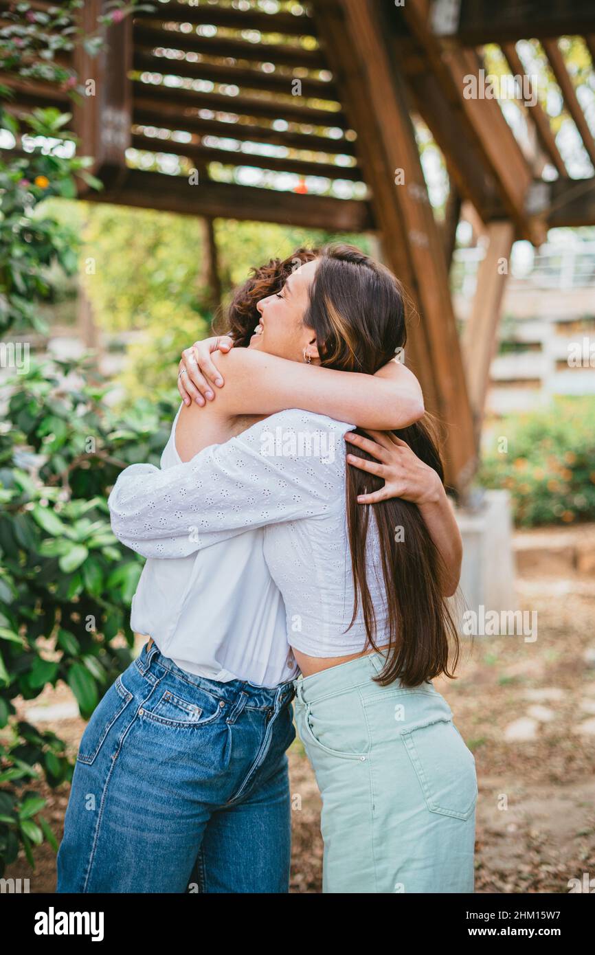 Two girl friends hugging each other surrounded by plants and bushes ...