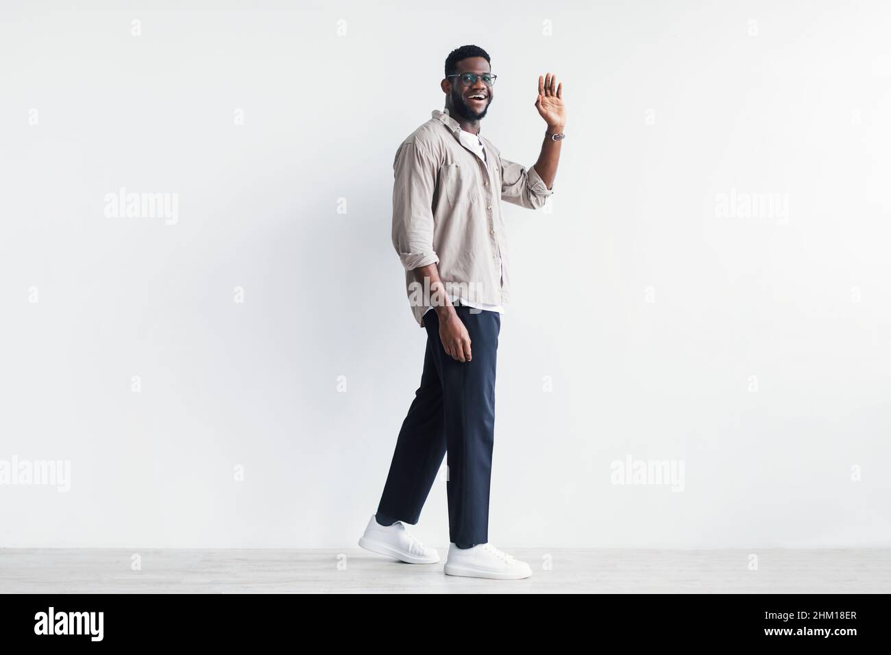 Handsome young black man walking and waving hand at camera, greeting ...