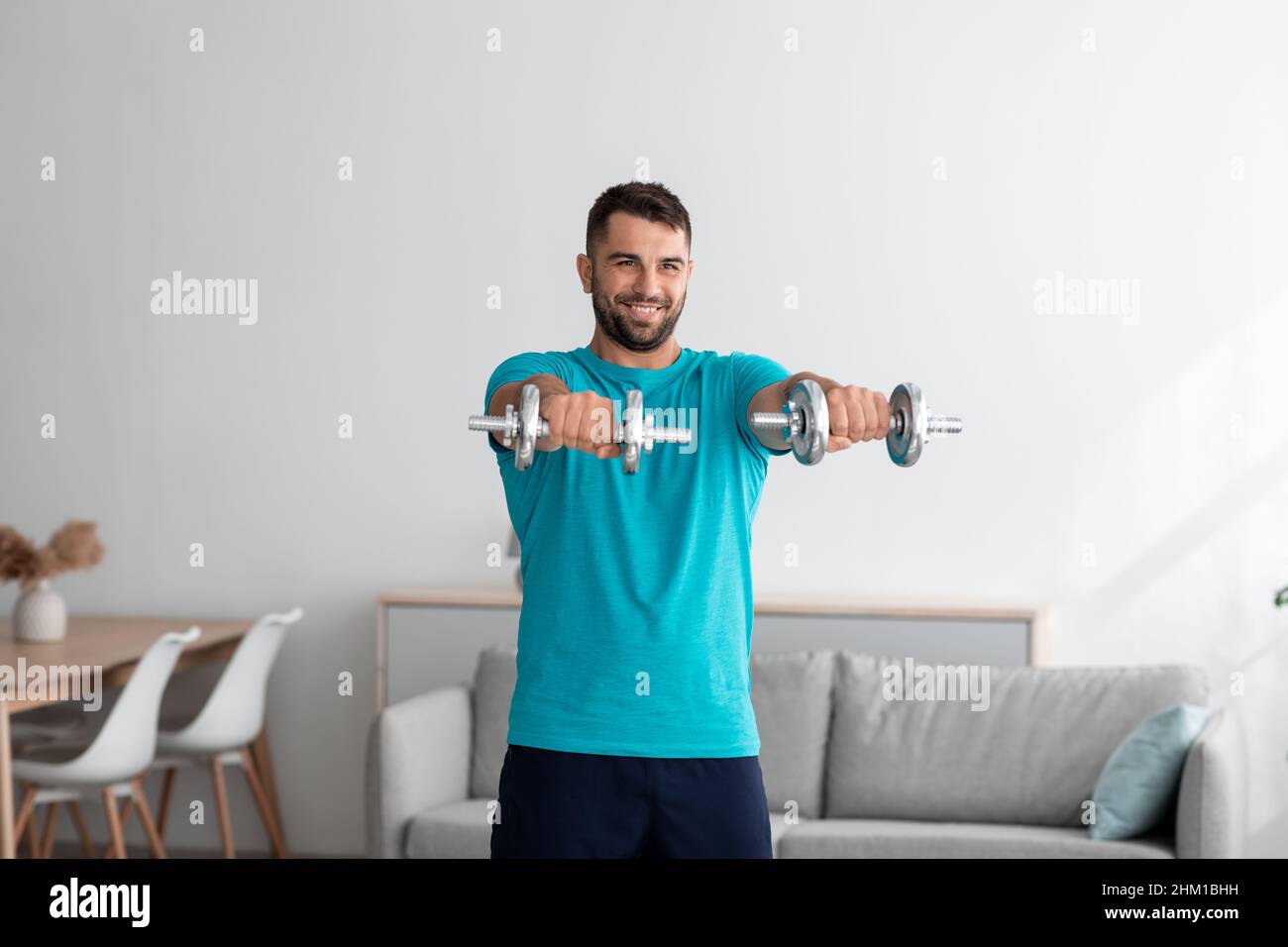 Glad Cheerful Millennial Muscular European Guy Doing Arm Exercises
