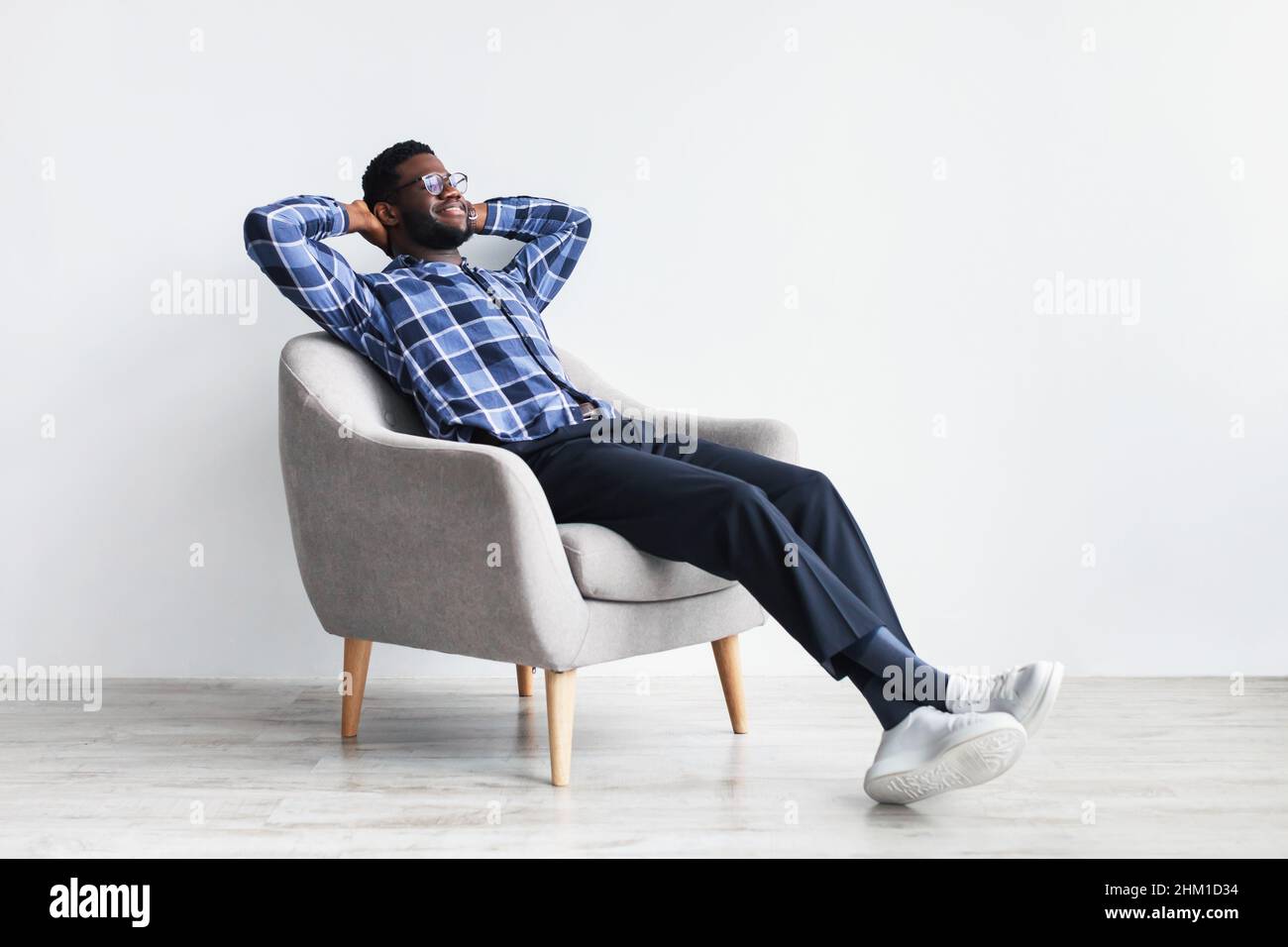 Peaceful young black man relaxing in armchair against white studio wall ...