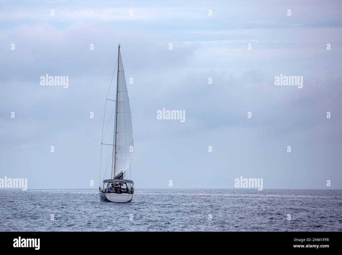Sailboat with open white sail rear view, cloudy sky and rippled sea ...