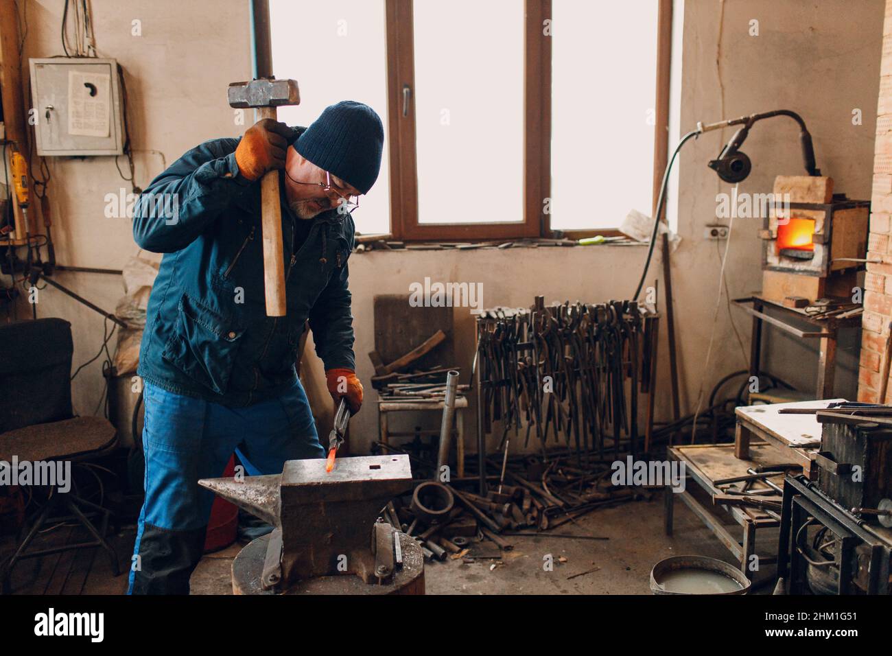 Blacksmith forges and makes metal detail with hammer and anvil at smith ...