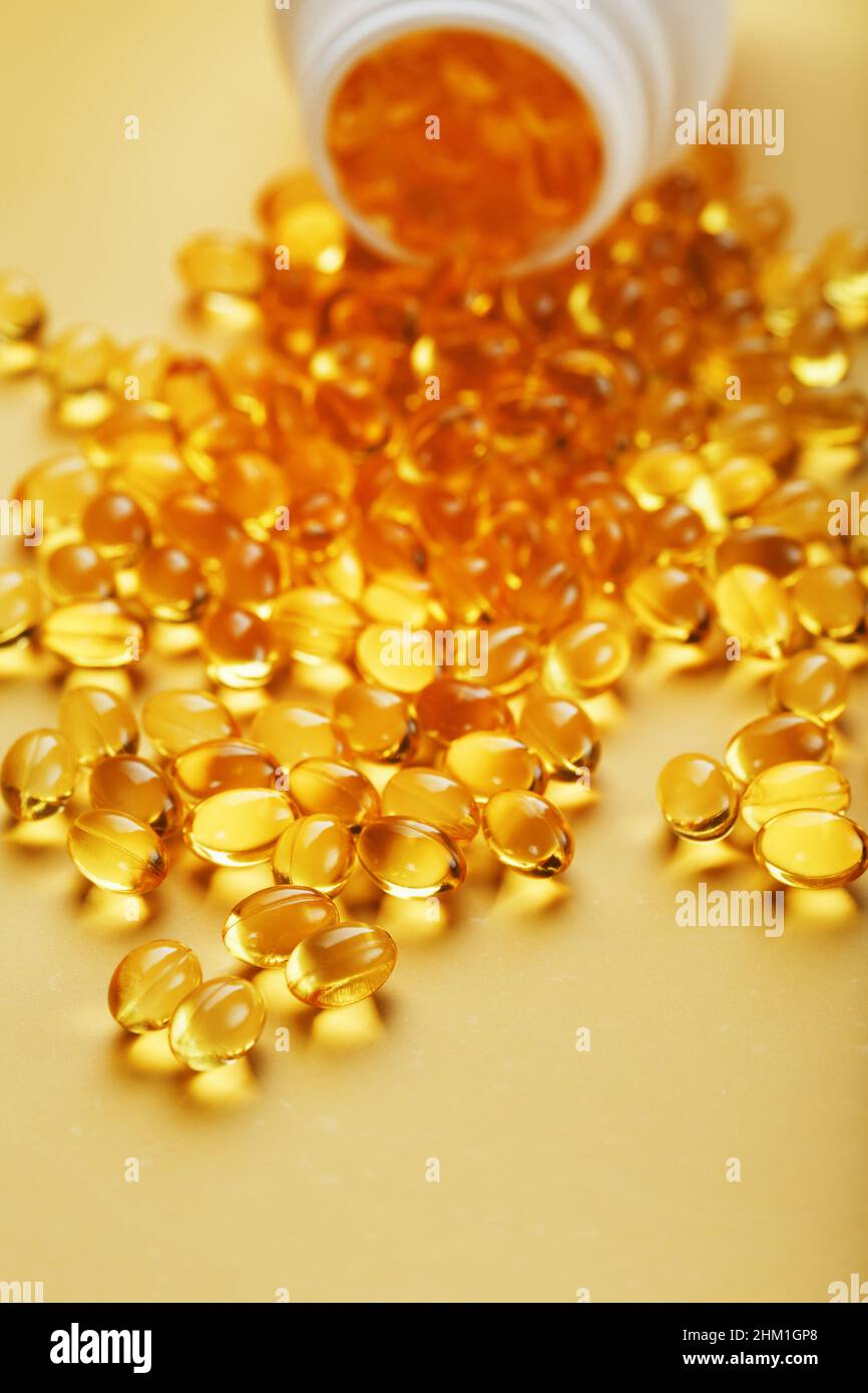 Gold Vitamin D3 capsules poured out of a jar on a yellow background ...