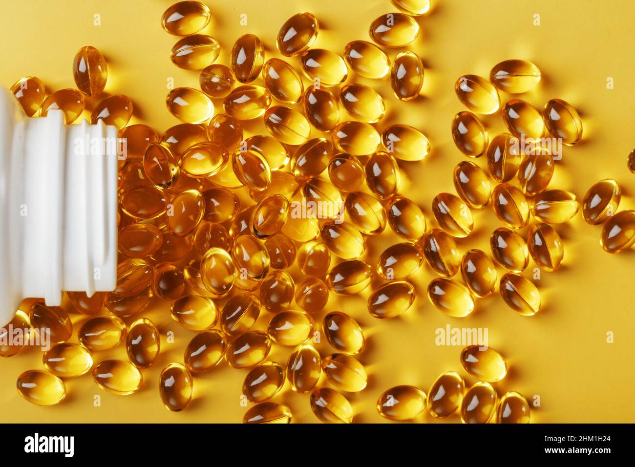 Gold Vitamin D3 capsules poured out of a jar on a yellow background ...