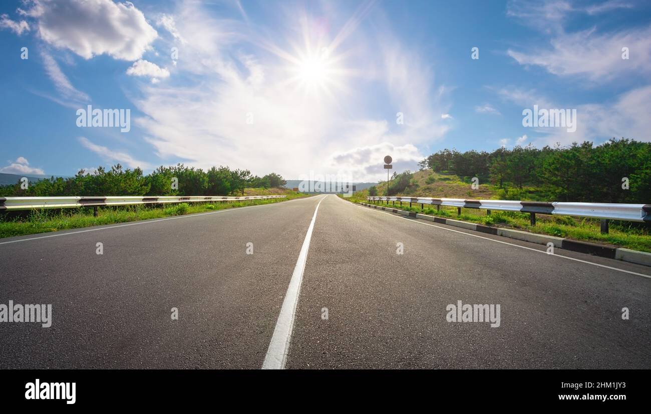 Asphalt highway with backlit sun on blue sky Stock Photo - Alamy