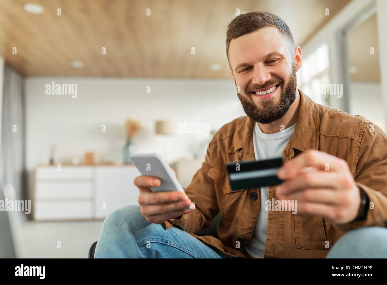 Happy Male Shopping Using Smartphone And Credit Card Sitting Indoors ...