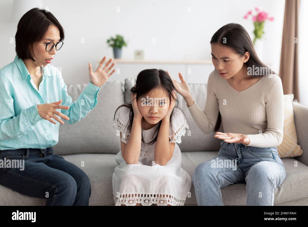 Unhappy Asian girl covering ears while angry mother and grandmother ...