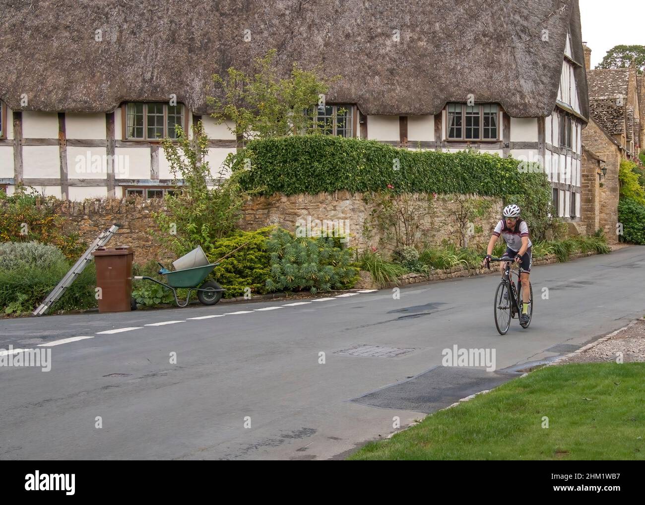 old thatched cottage with a cyclist cycling past Stock Photo - Alamy