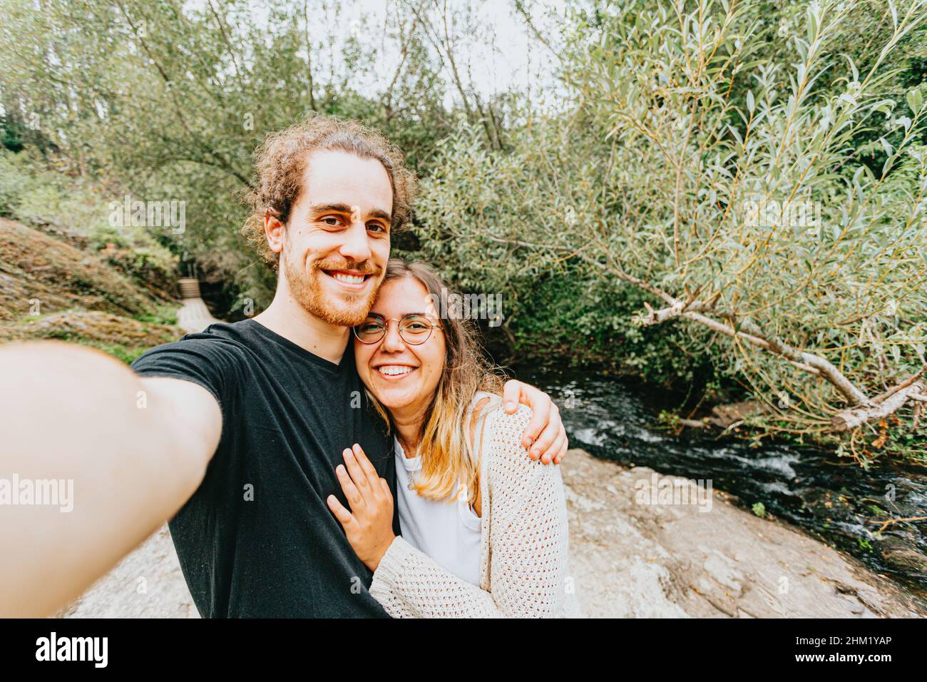 A young spanish couple taking a lovely selfie in the shore of a river ...