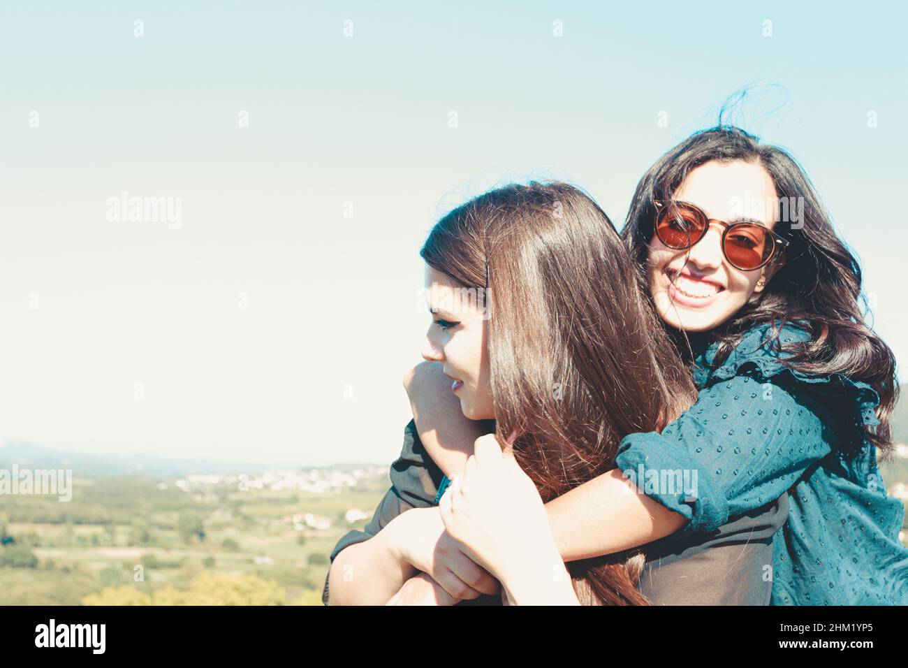 Two women hugging each other while one smiles to camera and uses ...