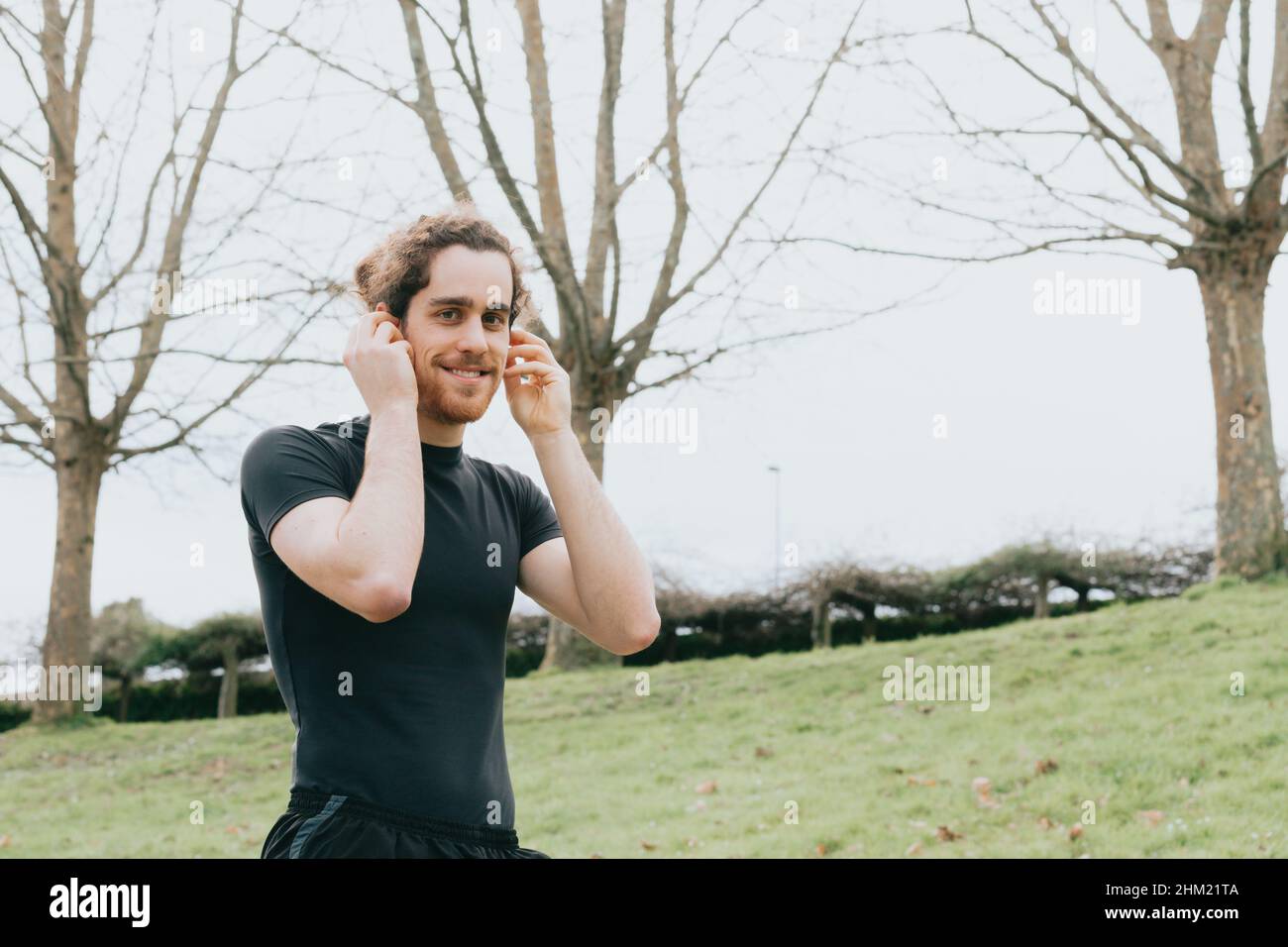 A young athletic male using headphones while doing exercise at the park ...