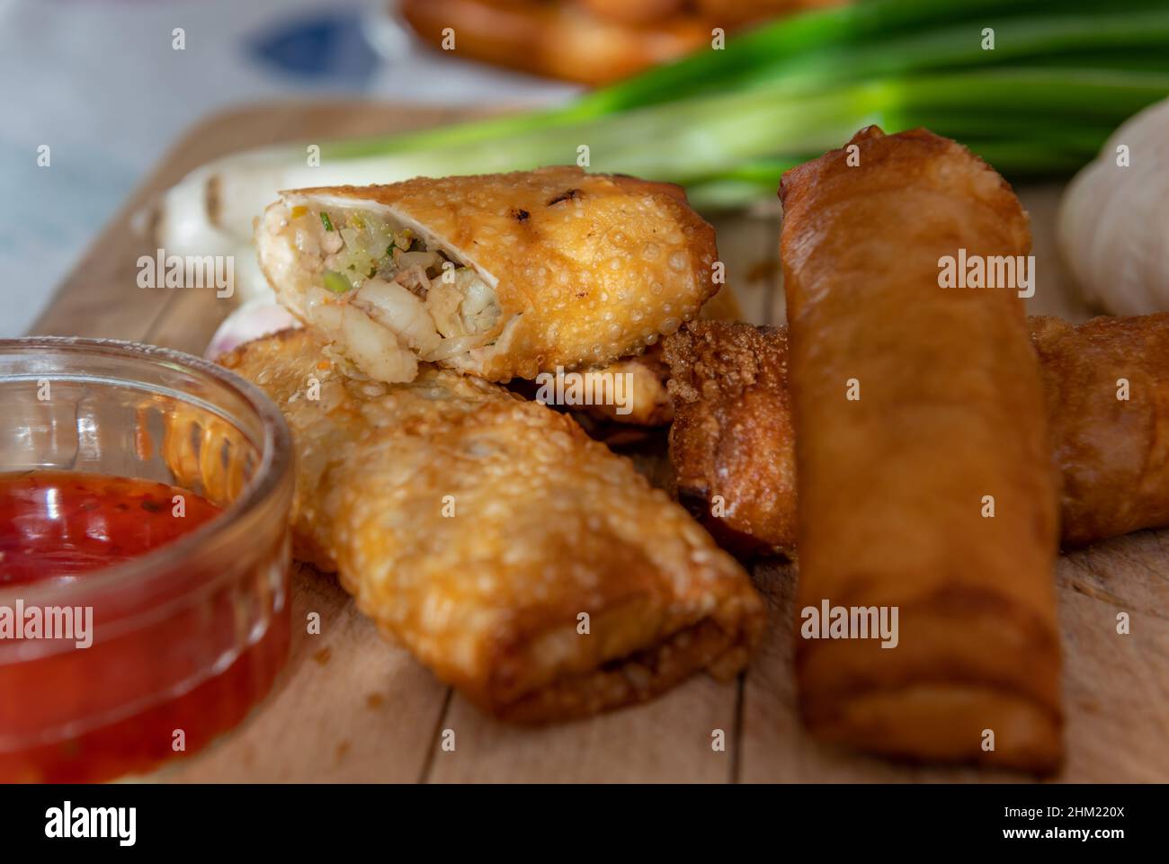 Crispy golden spring rolls on a wooden board with green onions and ...