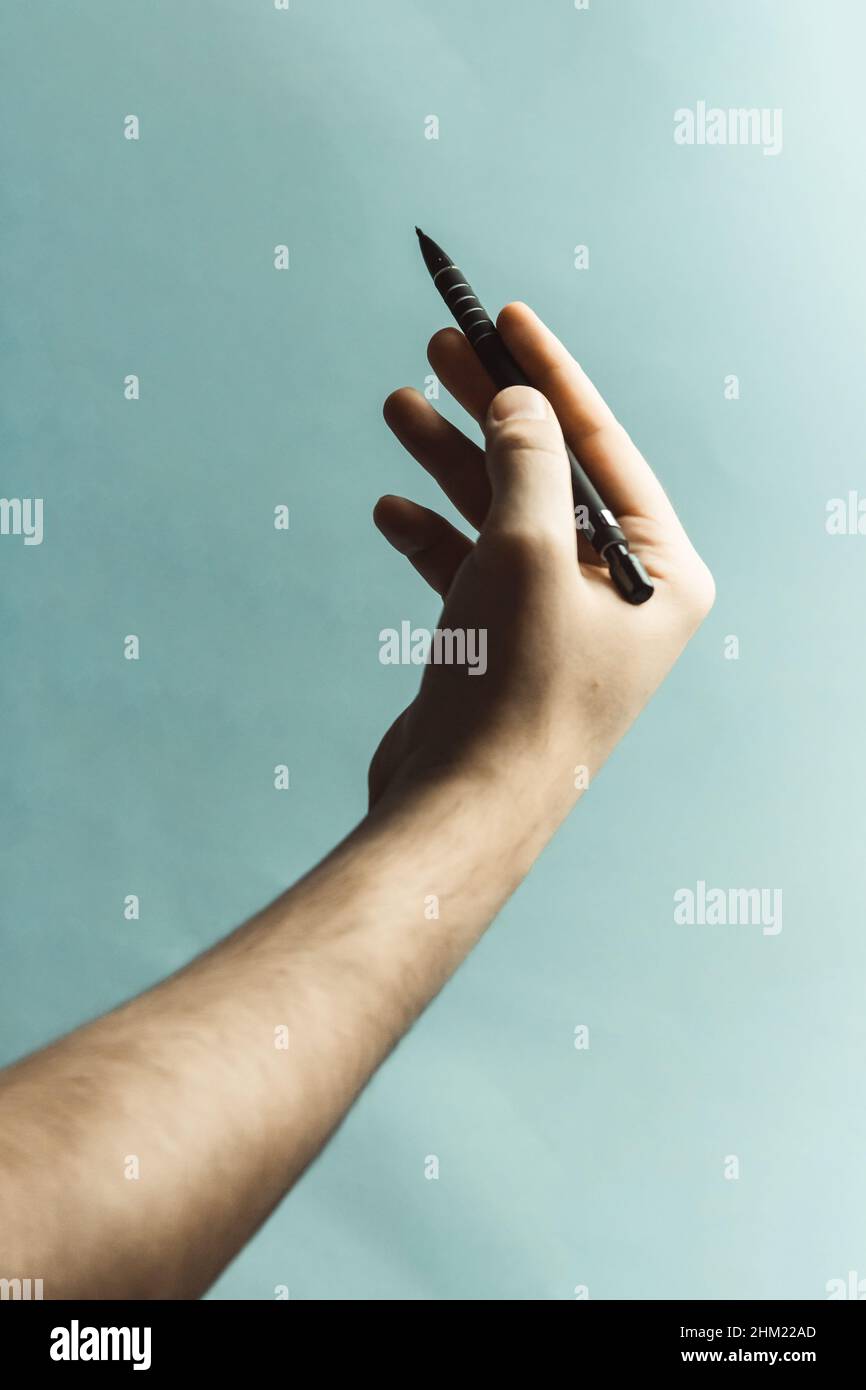 A young hand grabbing a mechanical pencil over a pastel blue background ...