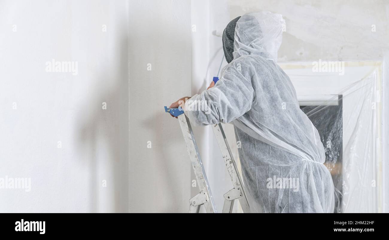 painter stands with paint roller on a ladder to paint the room window ...
