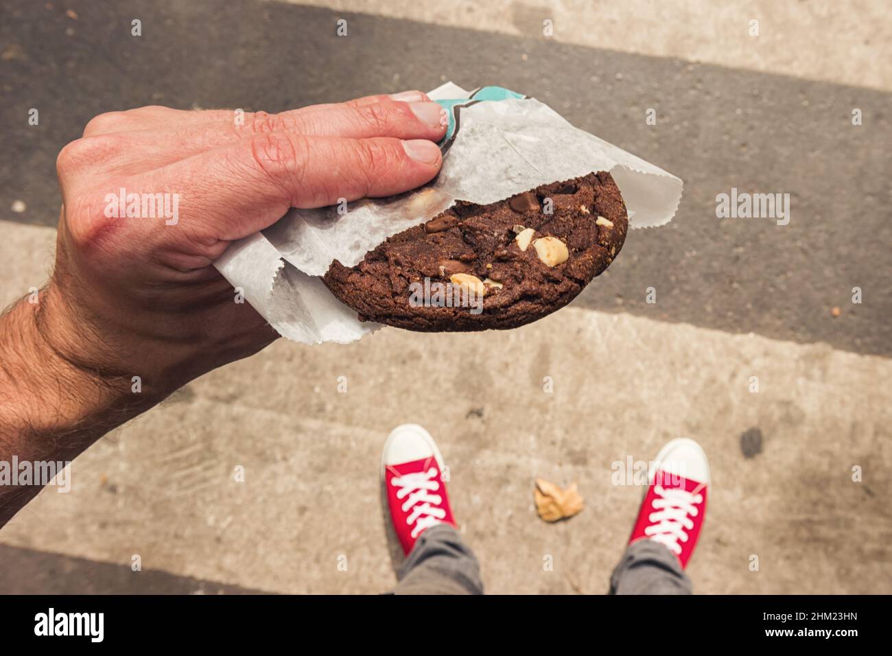 Male person standing on the street with fresh Chocolate Cookie in his ...
