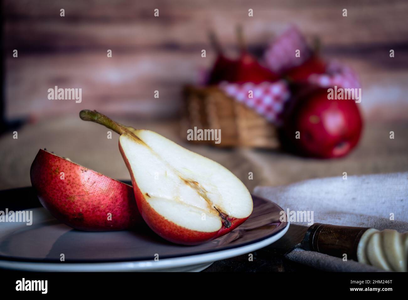 A red pear cut in half and other juicy red battler pears in a basket ...