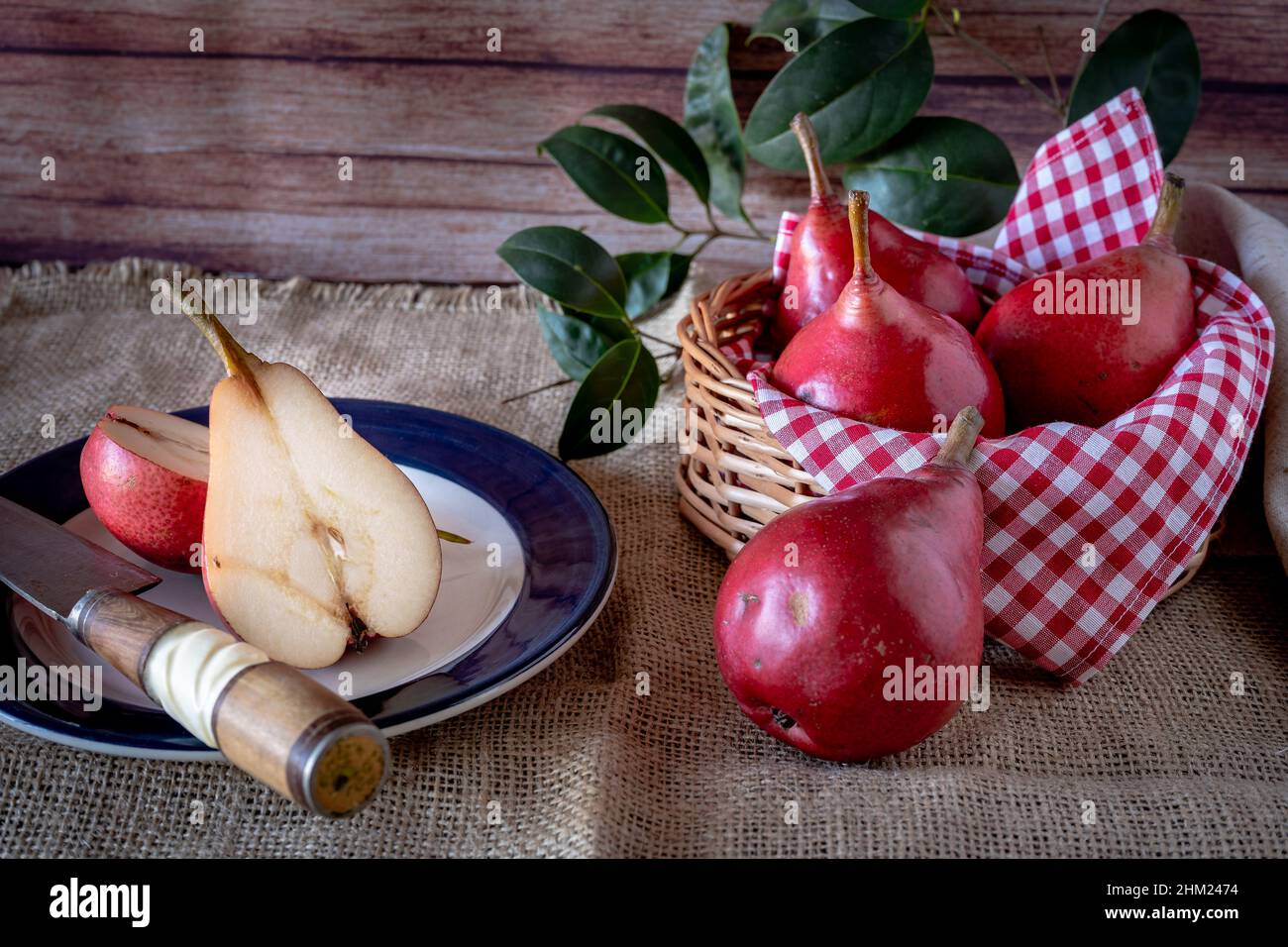A red pear cut in half and other juicy red battler pears in a basket ...