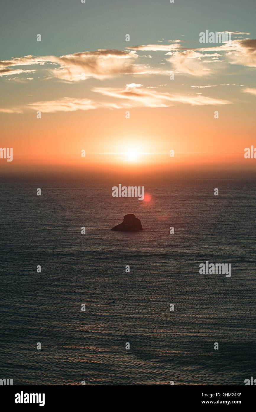 Massive sunset with sun flares over the ocean with a rock in the middle ...