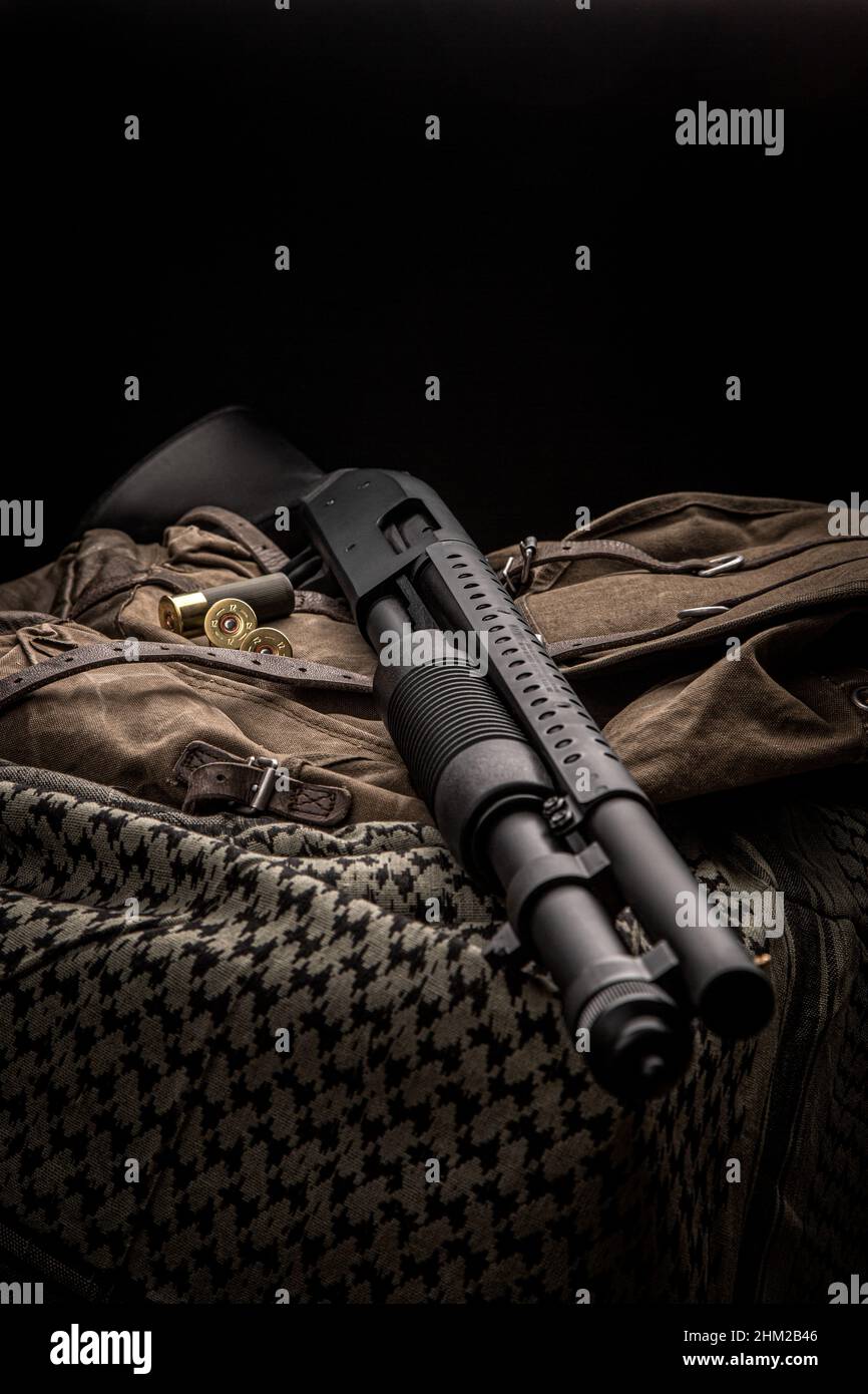 A black 12-gauge pump-action shotgun and ammo are on a canvas backpack ...