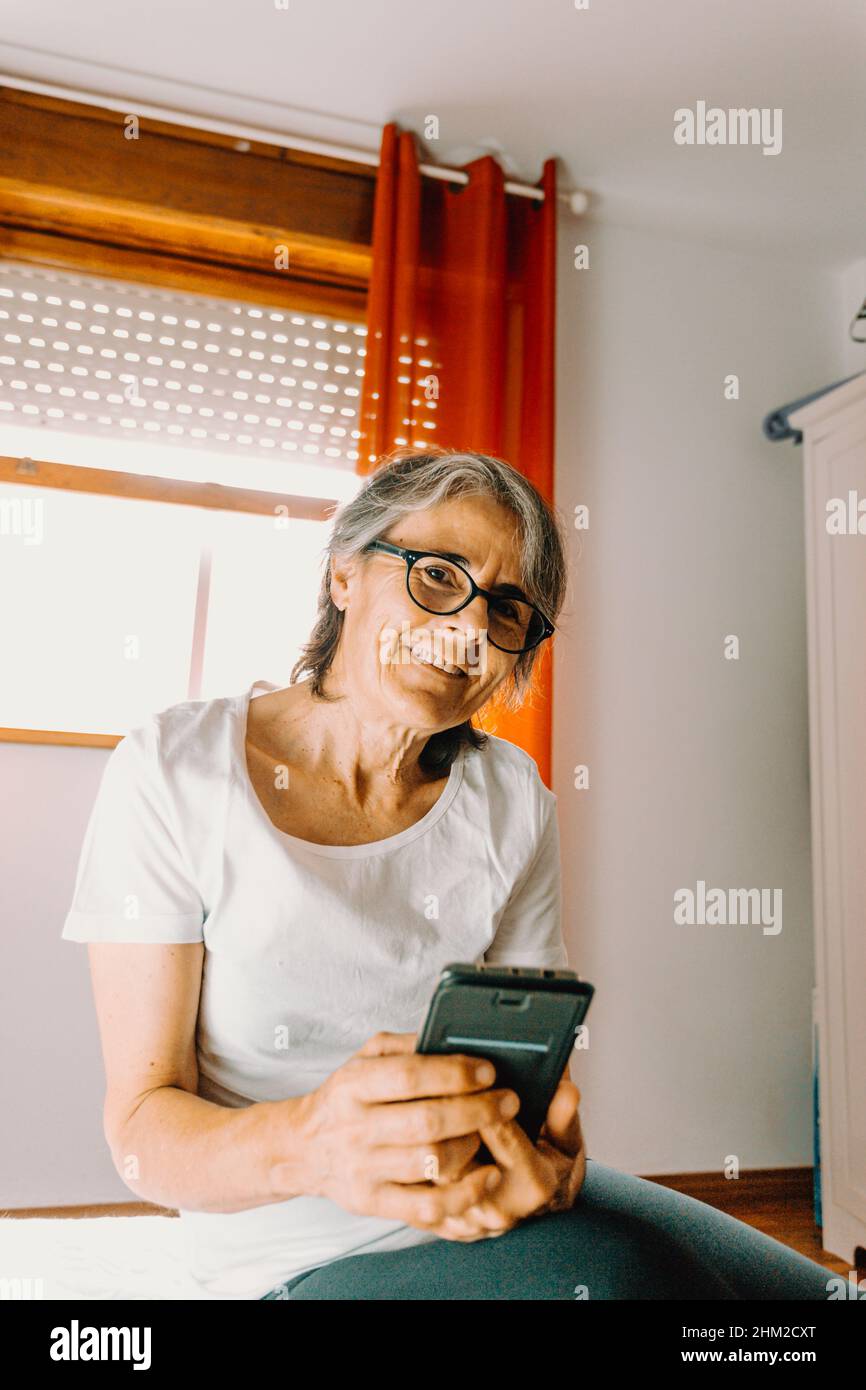A close up of an old female smiling to camera while grabbing his phone ...