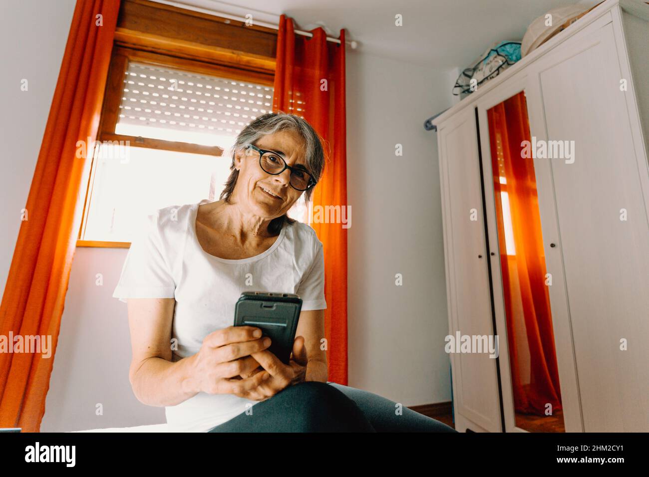 A close up of an old female smiling to camera while grabbing his phone ...