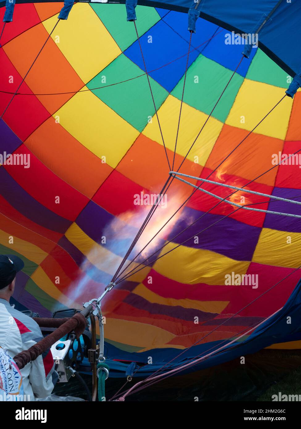 Partially-visible pilot inflating a colorful hot air balloon with a ...