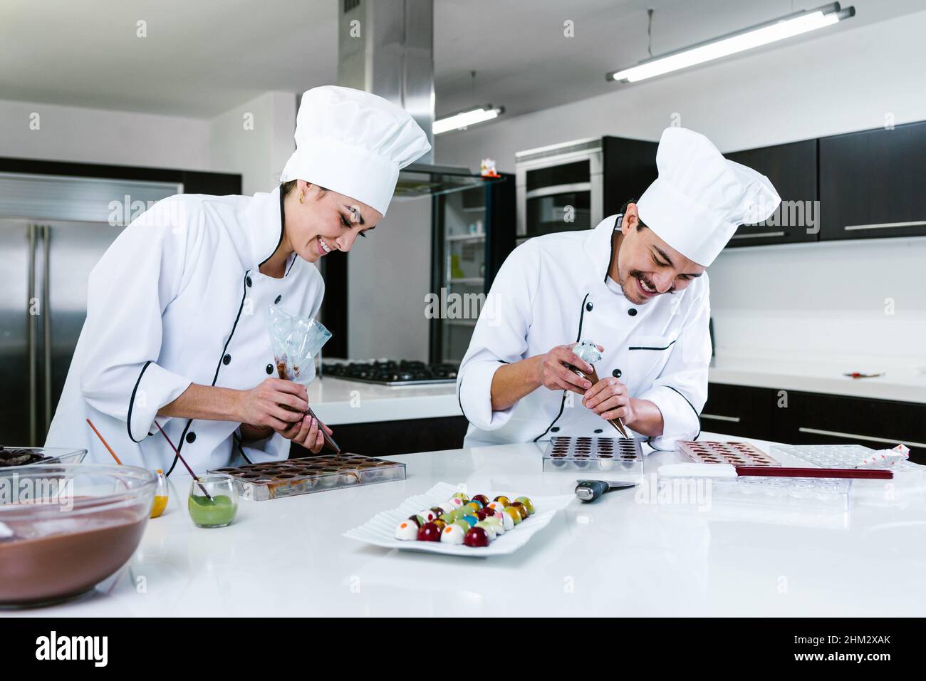 young latin couple woman and man chocolatier in chef uniform and hat ...