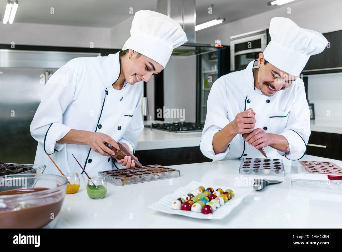 young latin couple woman and man chocolatier in chef uniform and hat ...