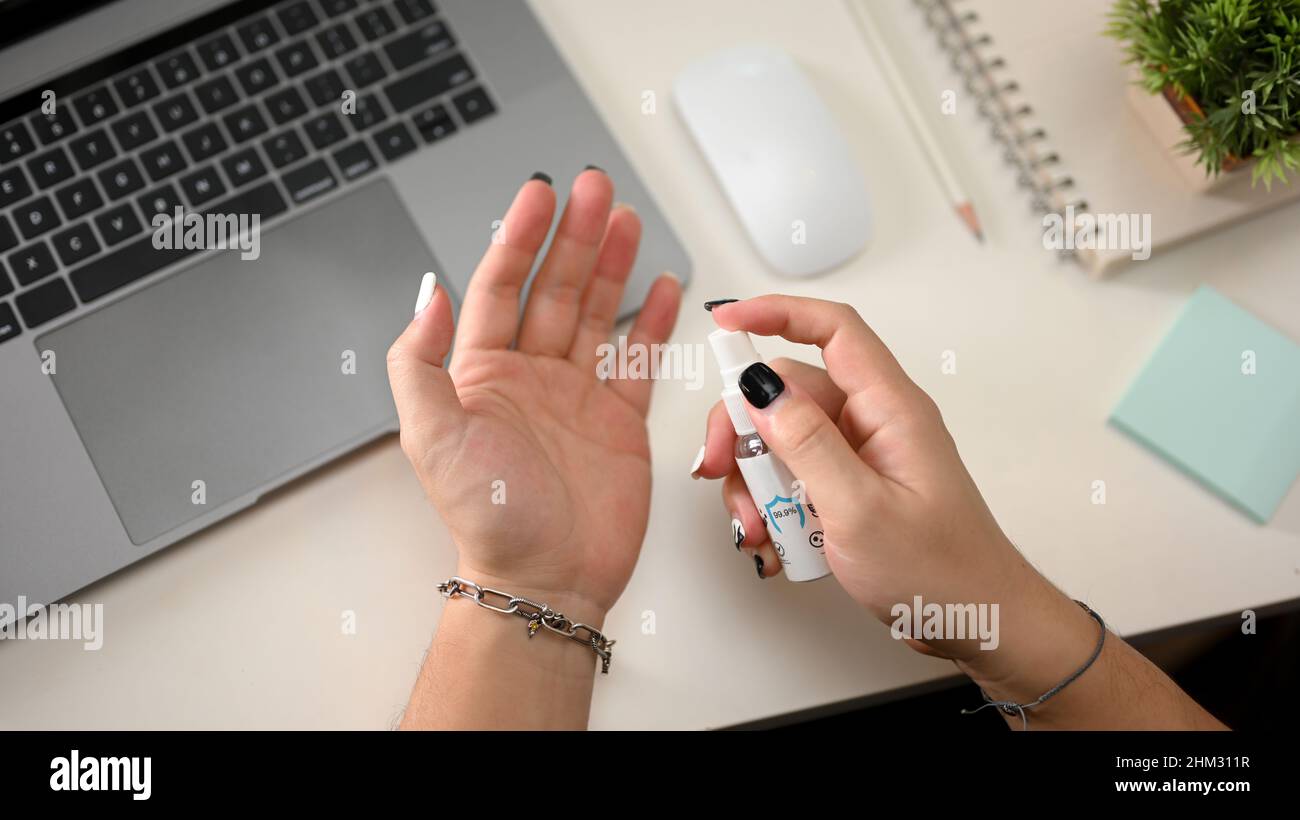 A woman uses hand disinfectant or sanitizer spray over her office desk ...