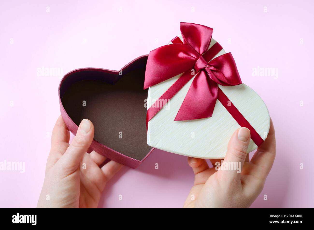 Woman's hands open the gift box on pink background, top view. Empty ...
