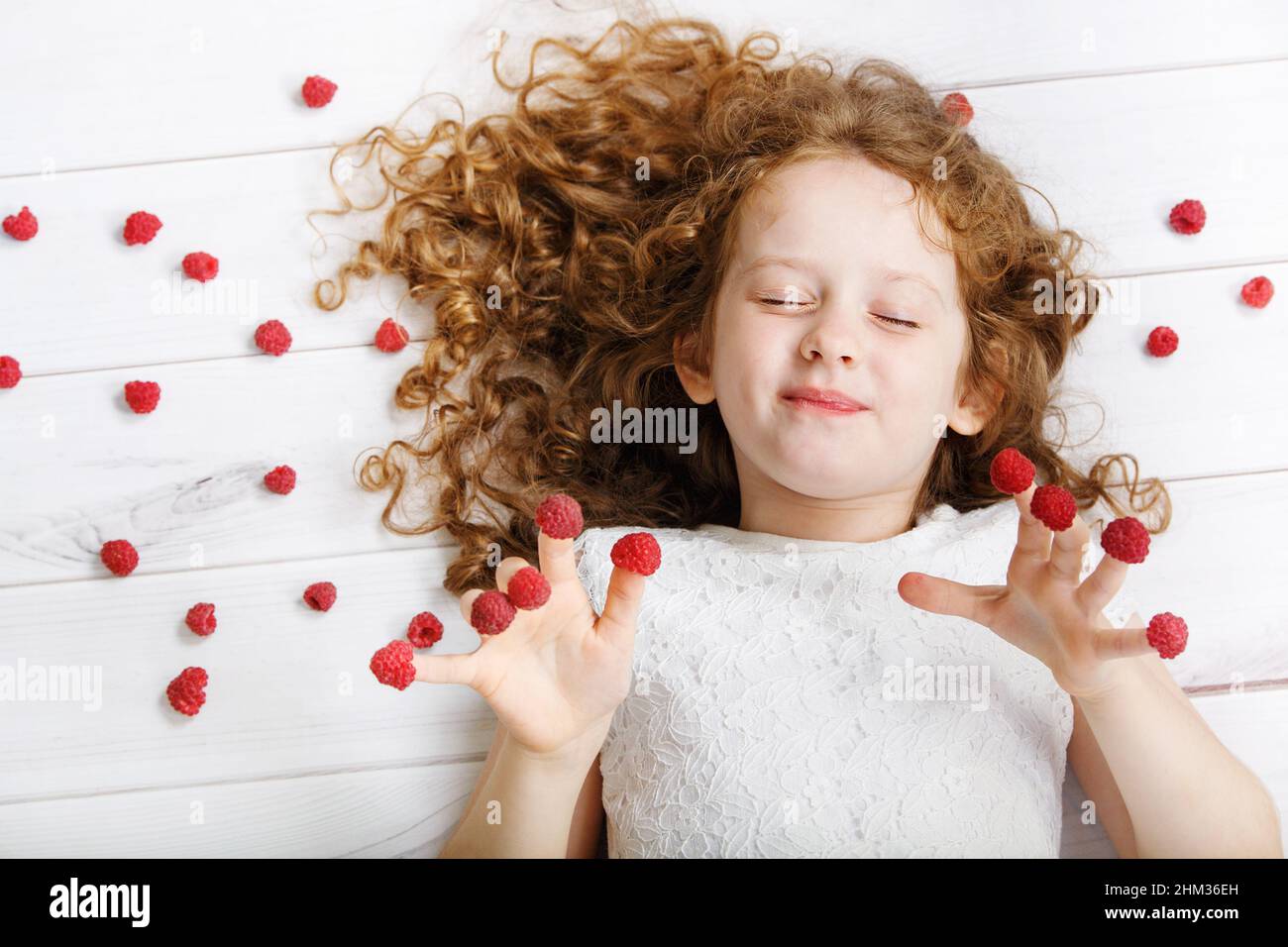 Cute girl enjoying closing her eyes and eating raspberries on his ...