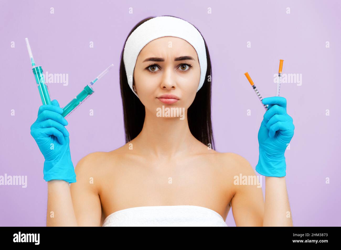 Portrait of a beautiful pensive young woman holding four syringes for ...