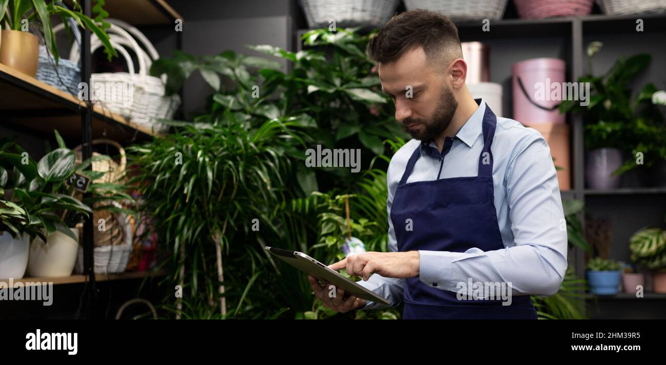 a flower seller in a flower center works on a tablet against the ...