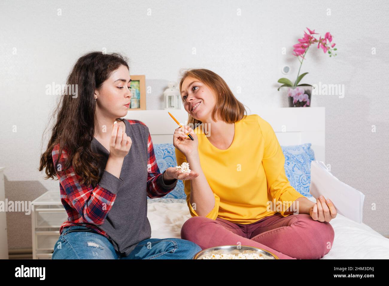 Two young women are sitting on the bed, eating popcorn and writing ...