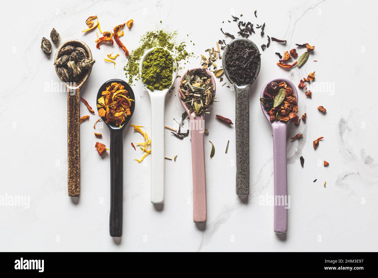 Various types of dry tea in spoons on a white marble background, top ...