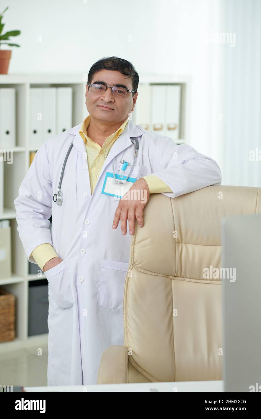 Portrait of confident smiling chief physician standing at his chair in ...