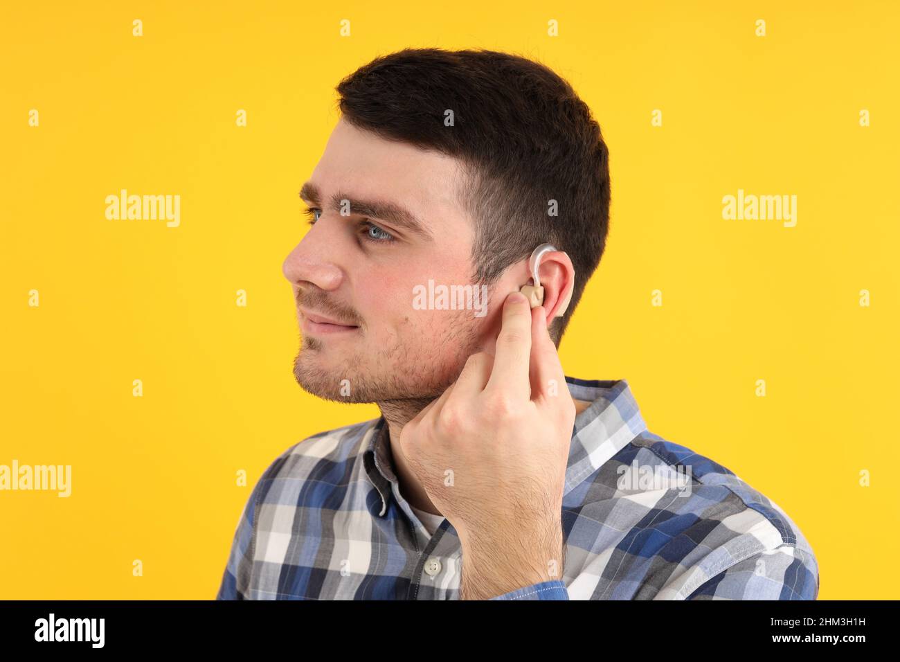 Young man with hearing aid on yellow background Stock Photo - Alamy