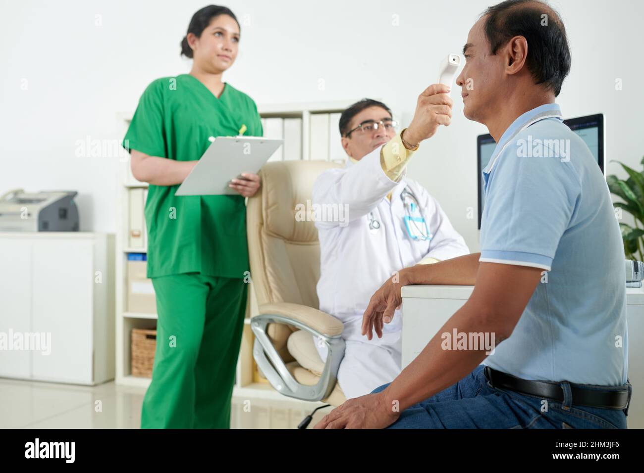 General practitioner measuring temperature of senior patient with ...