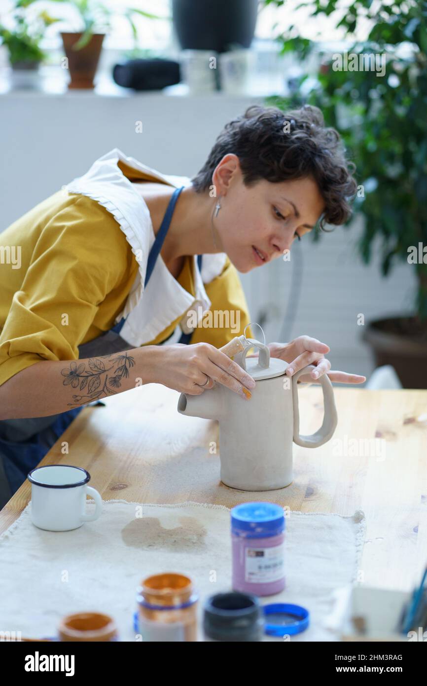 Young woman in apron learning how to make ceramics during masterclass ...