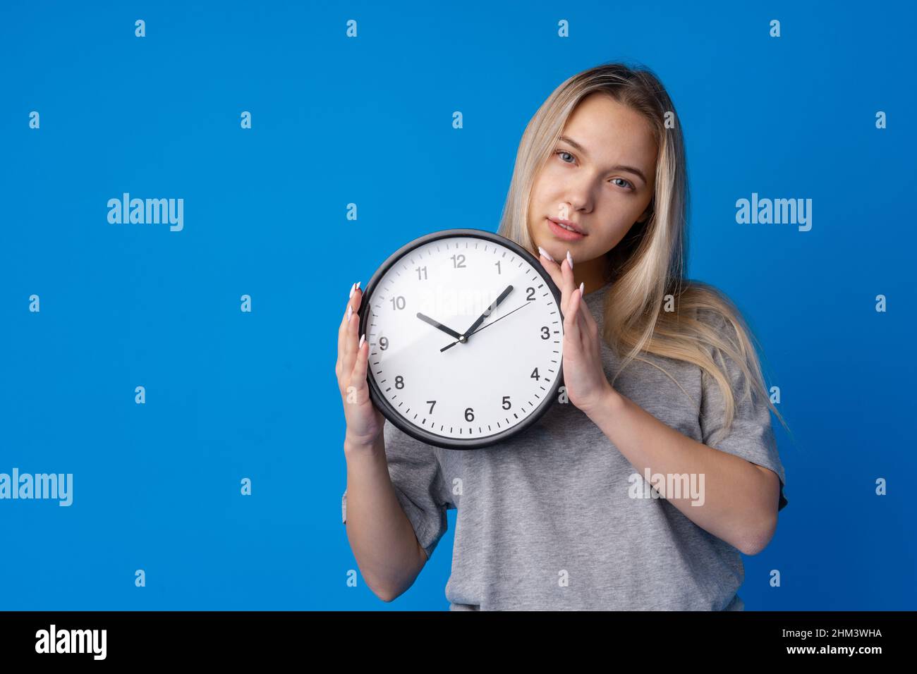 Beautiful teen girl holding wall clock over blue background Stock Photo ...